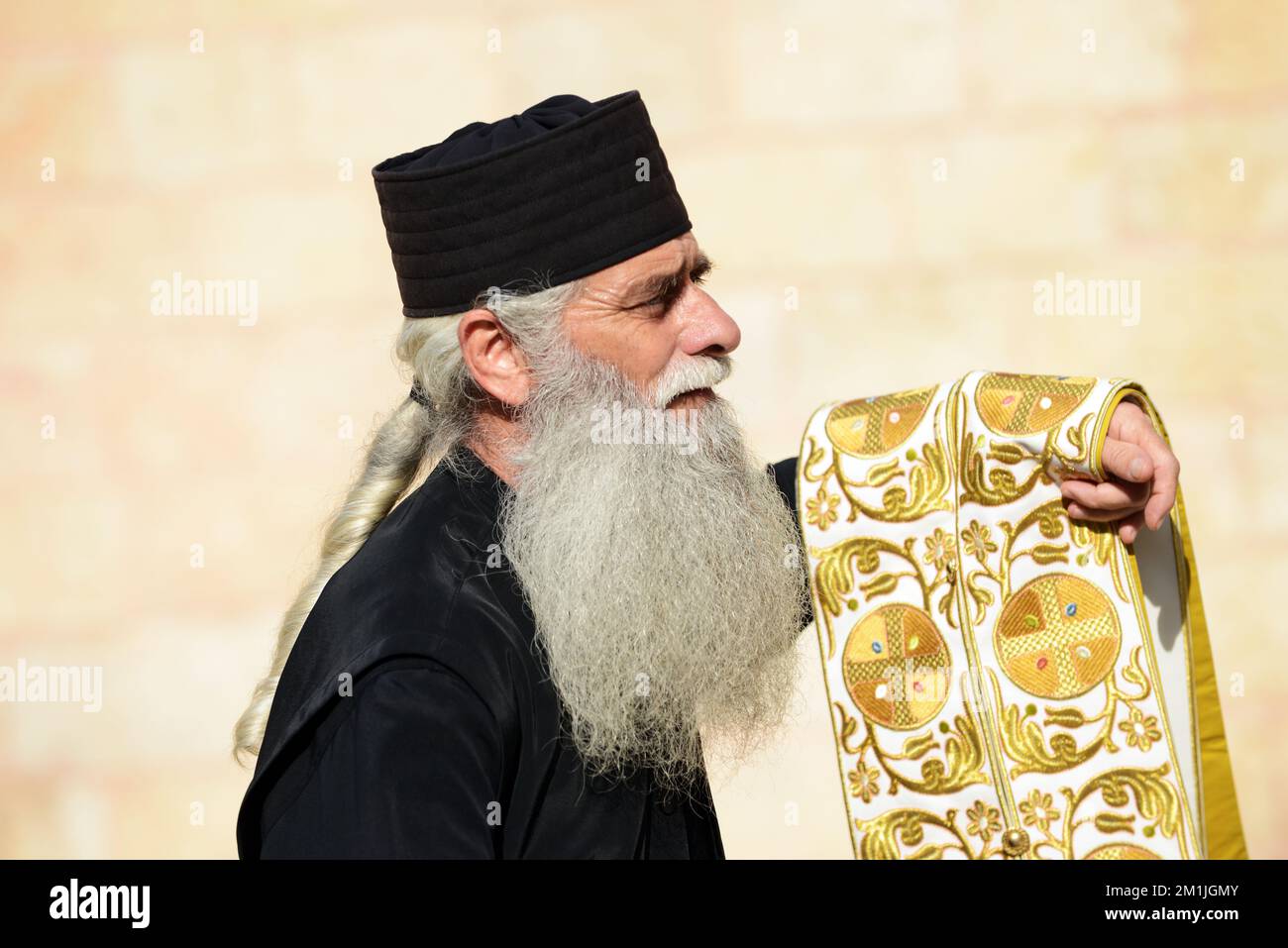 A Greek Orthodox priest holding a colorful tadeonal garment in ...