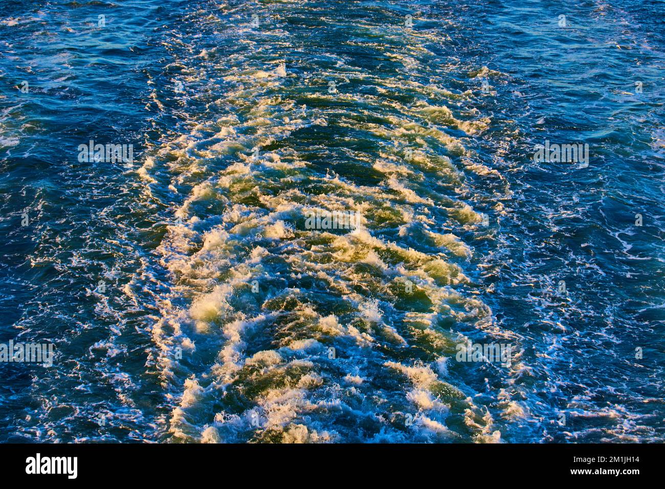 Raging waters from ferry boat looking down on waves with golden light ...