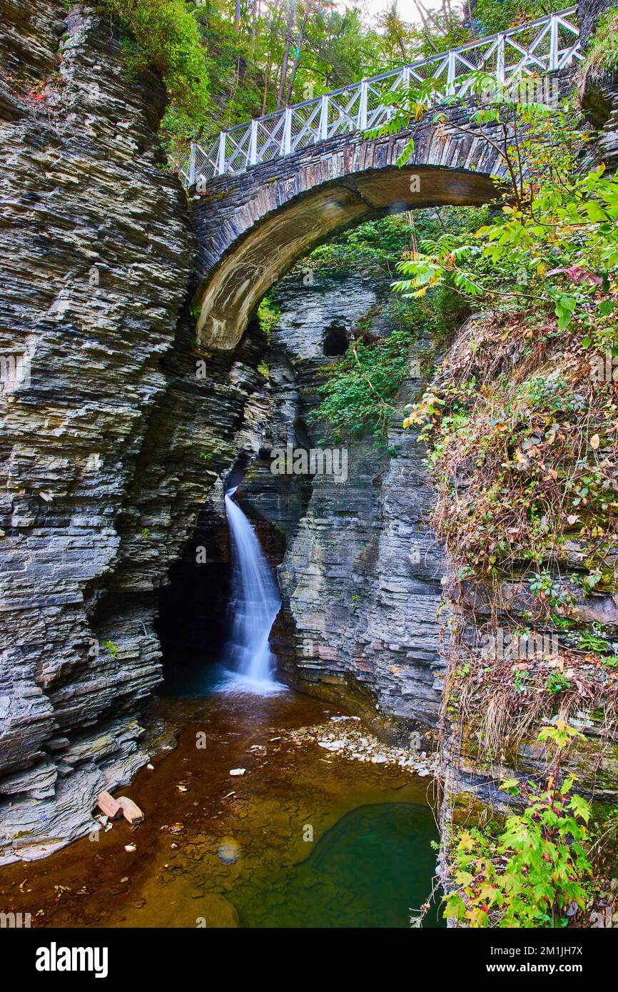 Stone bridge crosses over waterfall in deep gorge with layered rocks ...