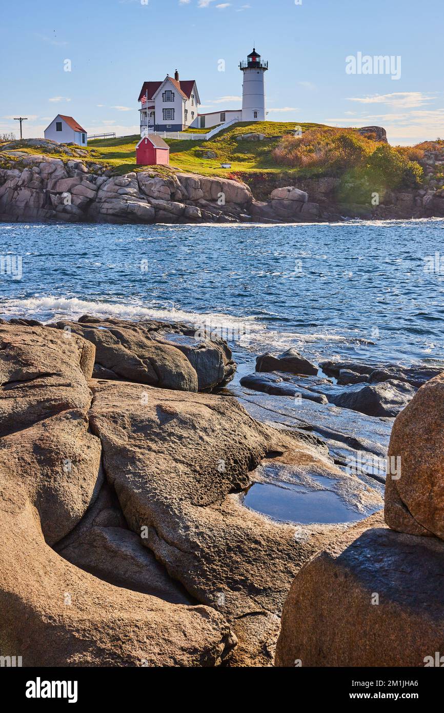 Lighthouse on island from mainland with boulders and puddles Stock ...