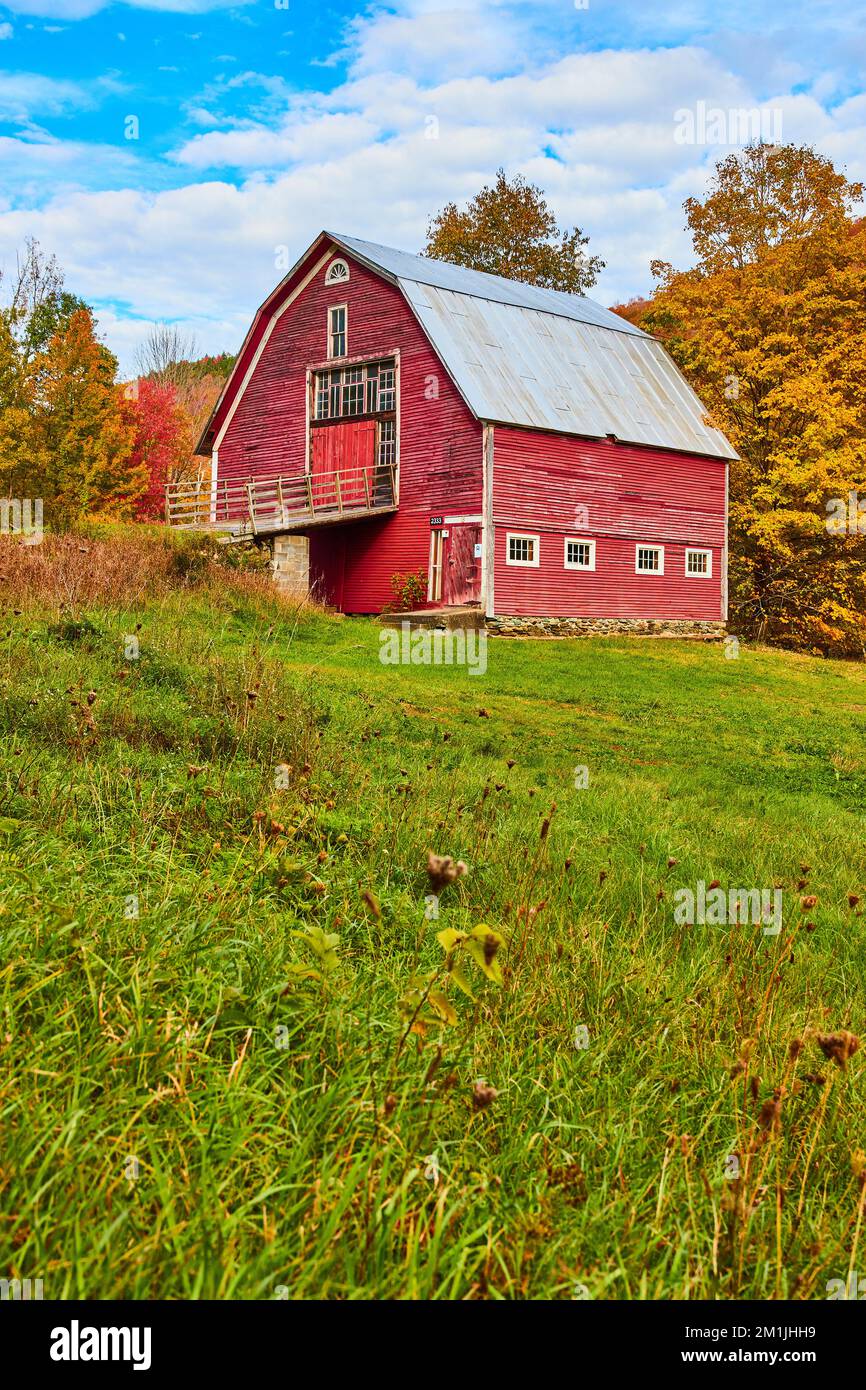 Large red vintage country barn in grassy fields with fall trees behind ...