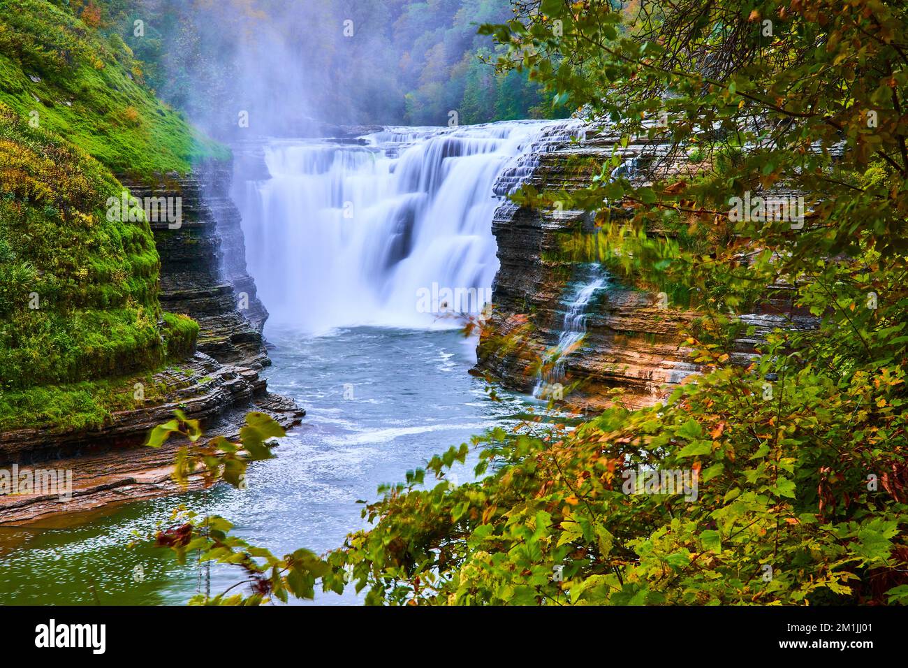Beautiful misty large waterfall through trees carving into rocky cliffs ...