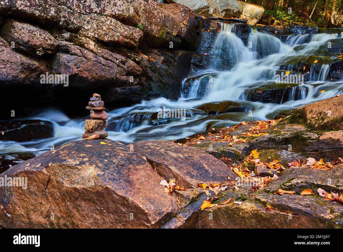 Small rock stack cairn on leaf-covered rocks along cascading river ...