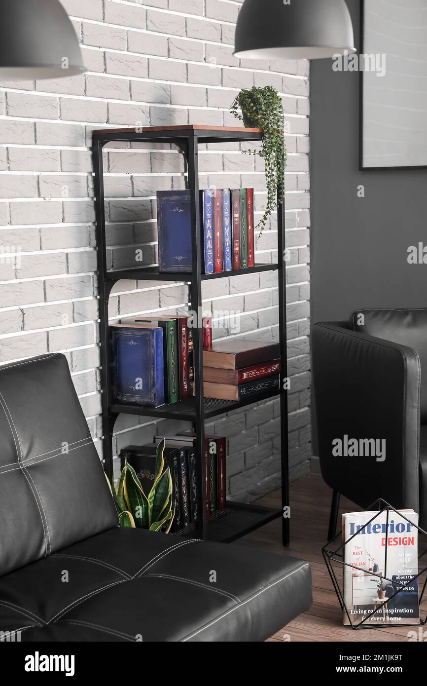 Shelf unit with books near grey brick wall in library interior Stock ...