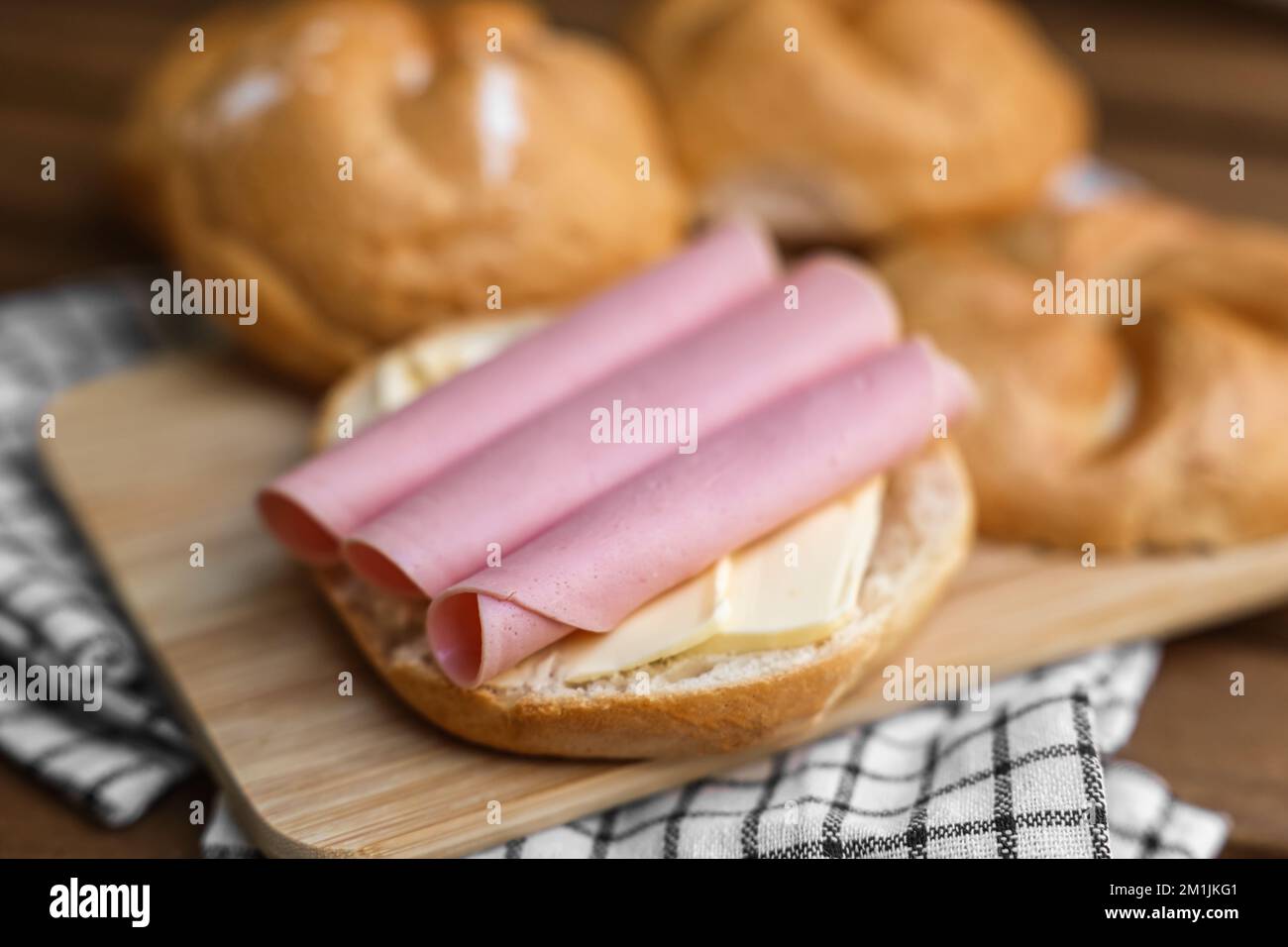 Delicious kaiser rolls with butter and ham on wooden board Stock Photo ...