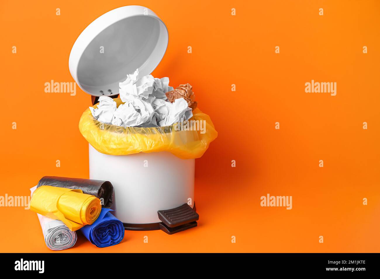 Open rubbish bin with crumpled paper and garbage bags on color ...
