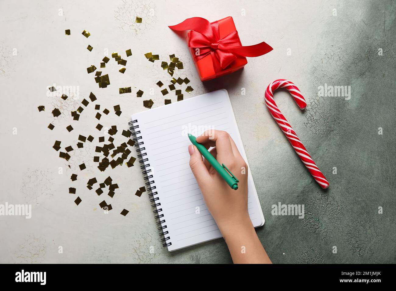 Female hand with notebook, pen, Christmas gift, candy cane and confetti ...