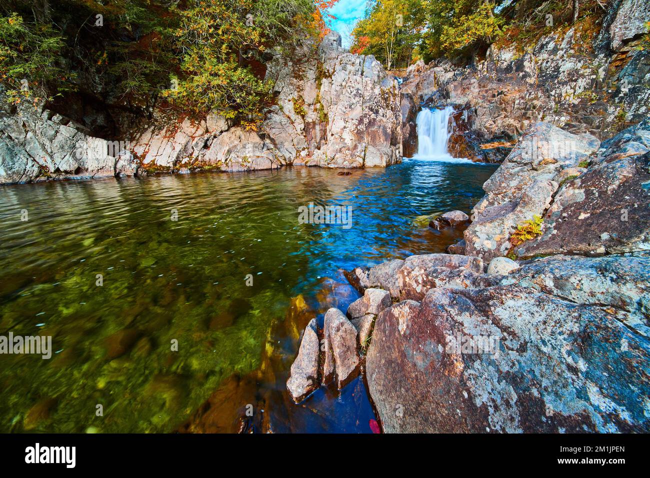 Small waterfall over rocks into blue and green river next to huge ...