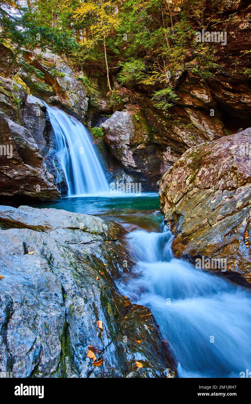 Looking up raging river through boulders with waterfall over mossy ...