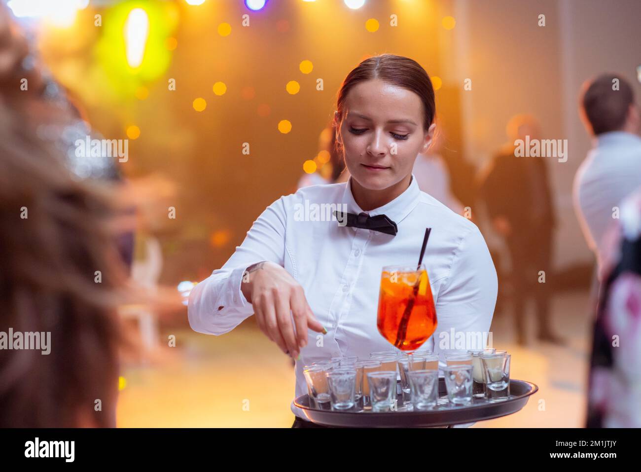 A preety young waitress serving drinks cocktails during a Party with colorful lights Stock Photo ...