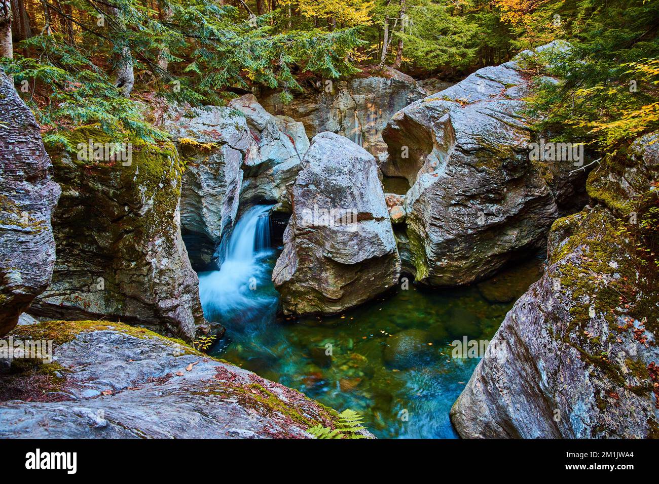 Magical waterfall into blue waters carving through huge rocks in mossy ...