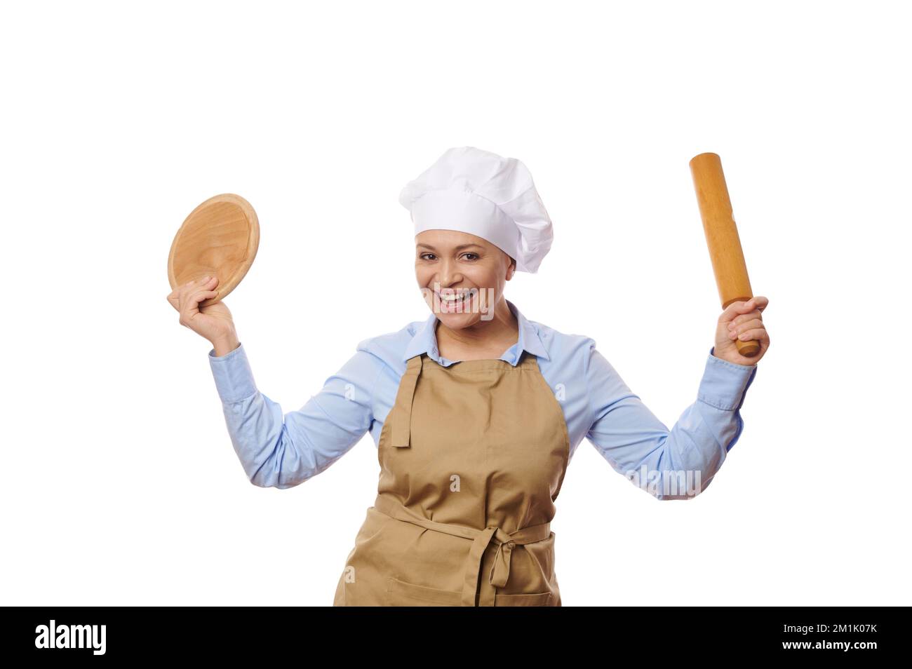 Cheerful Hispanic female pastry chef in beige apron, poses with rolling ...