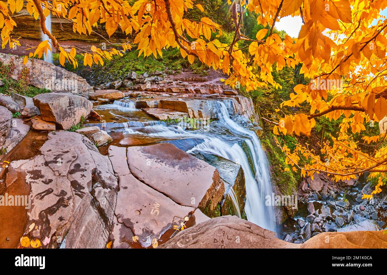 View through golden fall leaves of cliffs with waterfall right at top ...