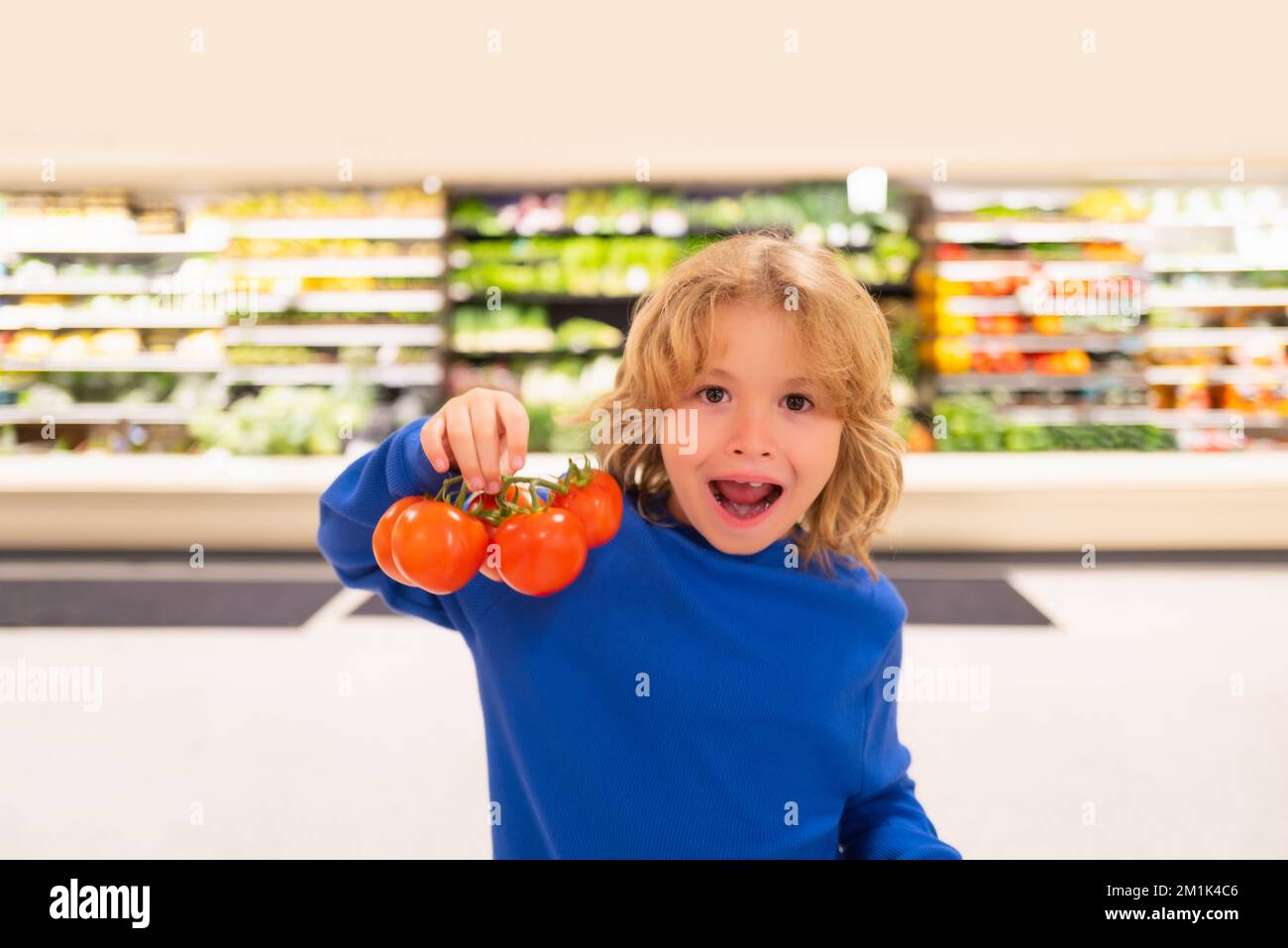 Child with fresh tomato vegetables. Kid choosing food in grocery store ...
