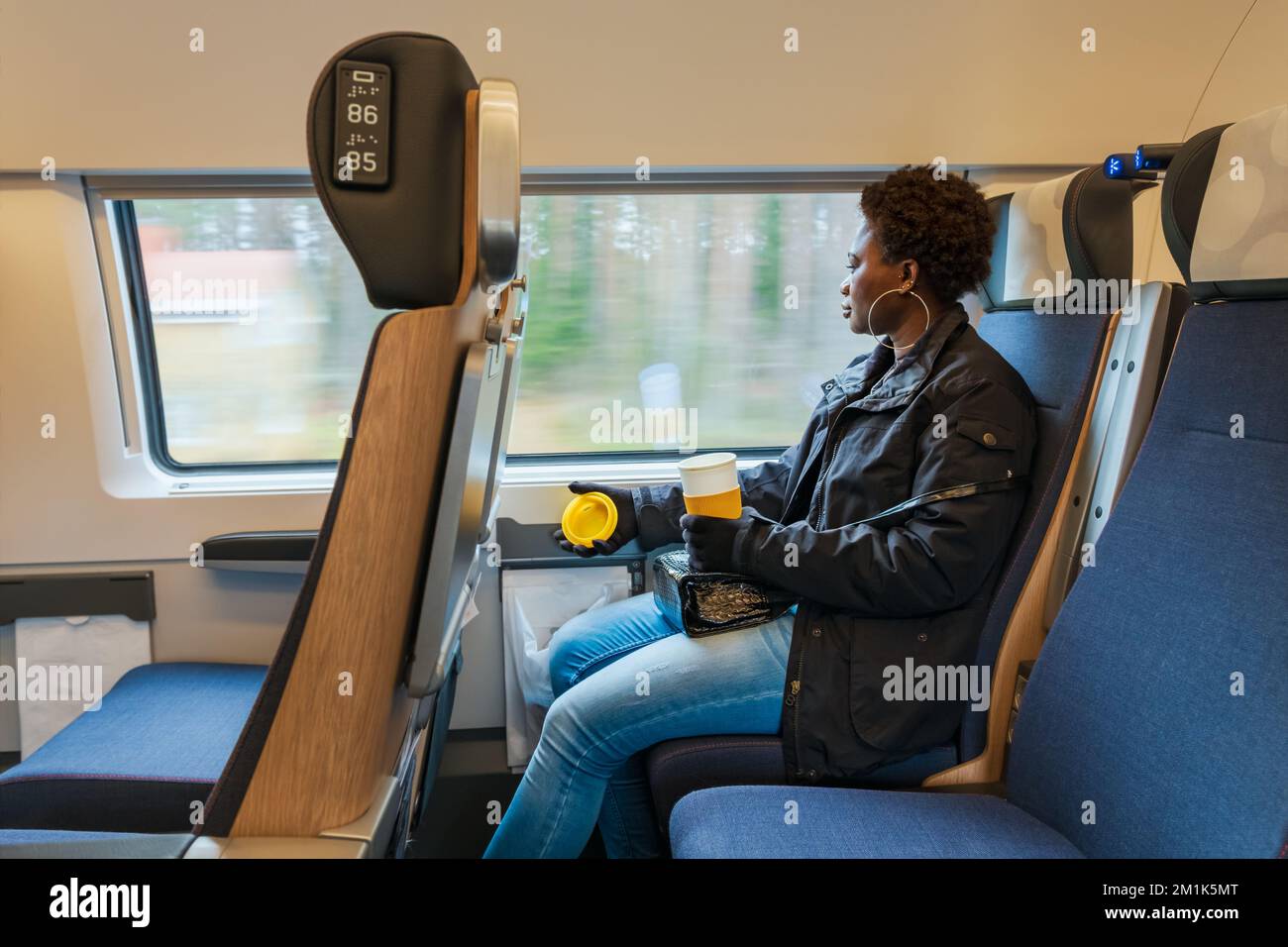 African woman sits on a commuter train in central Sweden with a cup of ...