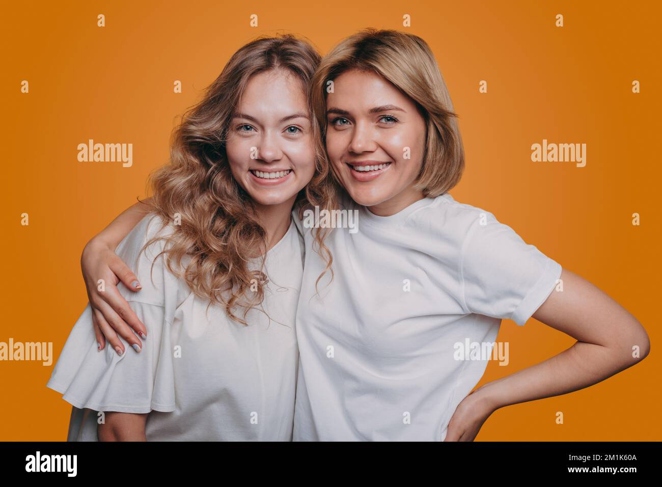 Two young women dressed in white t-shirts embracing and happy standing ...