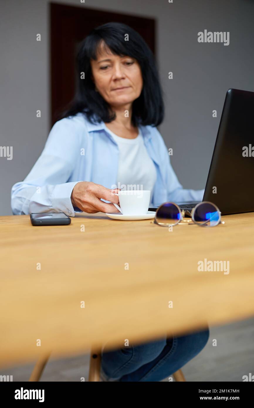Elderly lady businesswoman relaxing at workplace, drinking coffee while ...