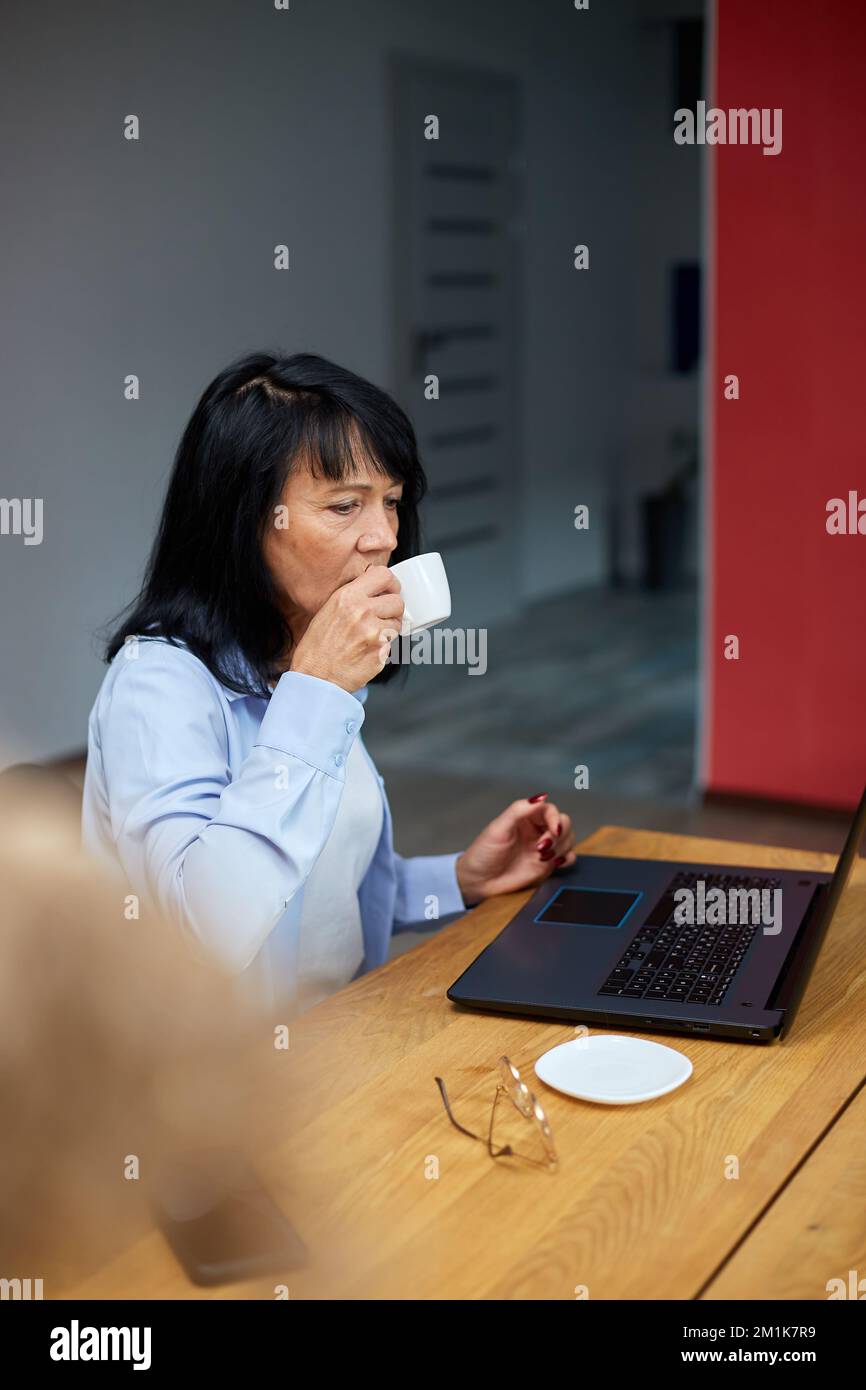 Elderly lady businesswoman relaxing at workplace, drinking coffee while ...