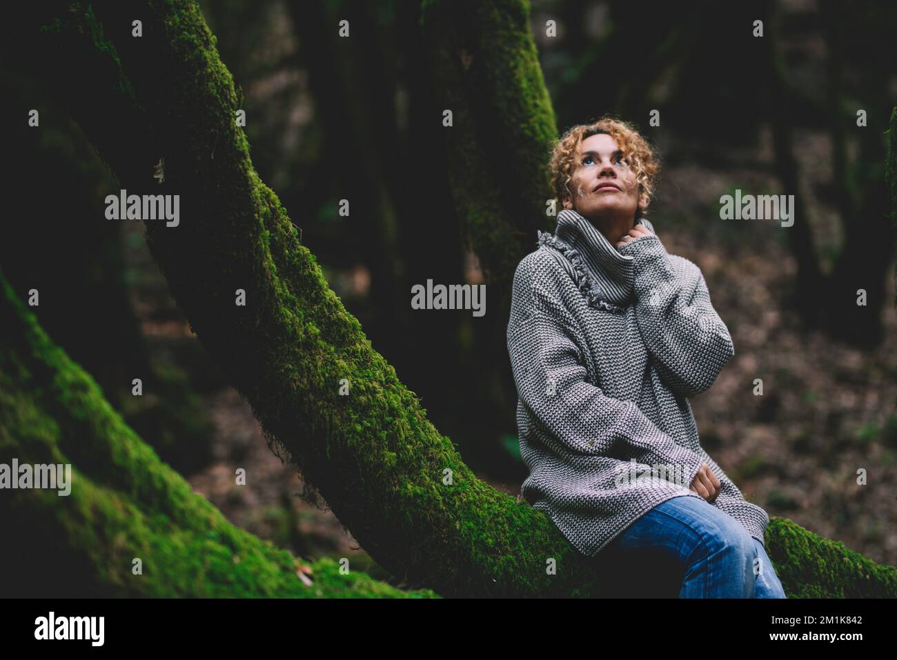 Serene woman sitting and relaxing on a green musk covered trunk in ...
