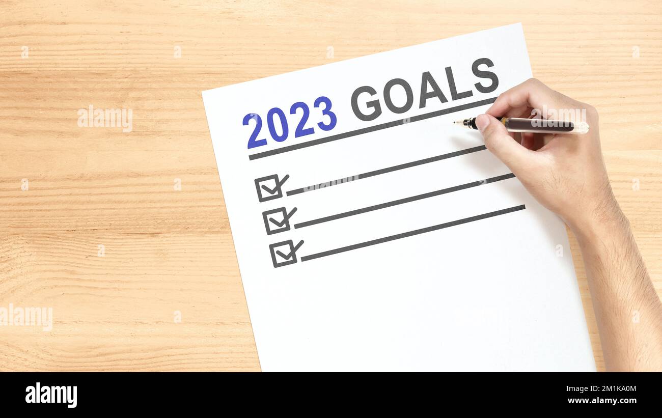 Human hand writing the 2023 goal list is on the note paper. Goals of ...