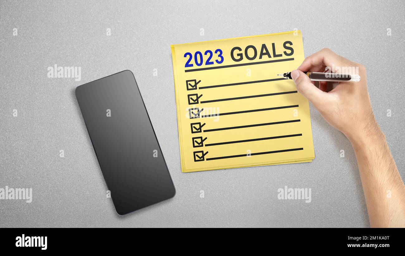 Human hand writing the 2023 goal list is on the note paper. Goals of ...