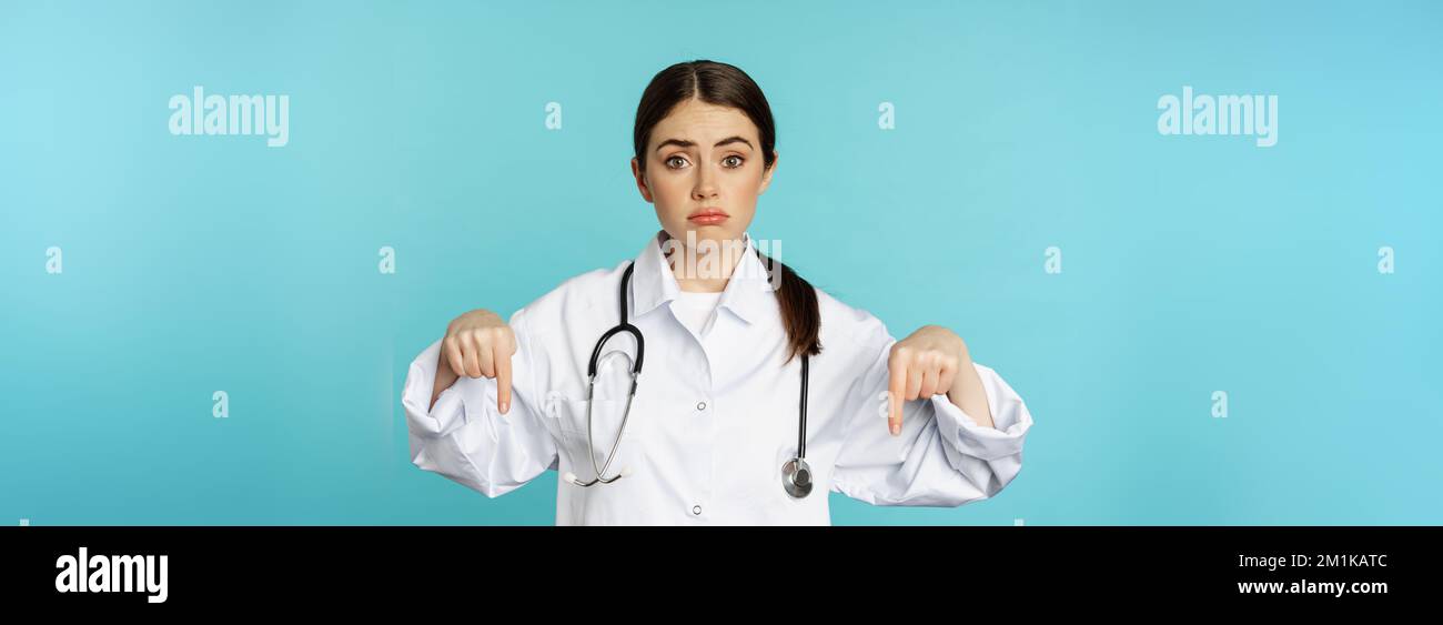 Sad and gloomy doctor, female medical worker pointing fingers down ...