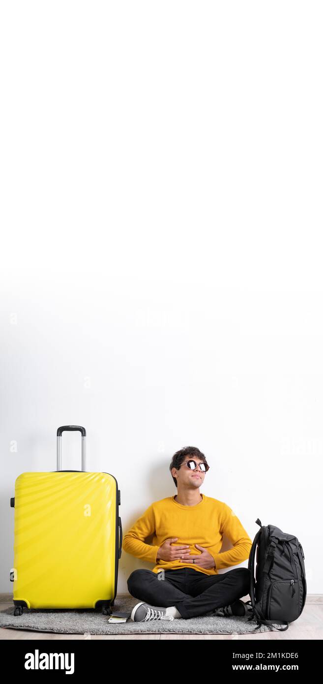 Sick traveler tourist with a suitcase sits holding hands on his stomach ...