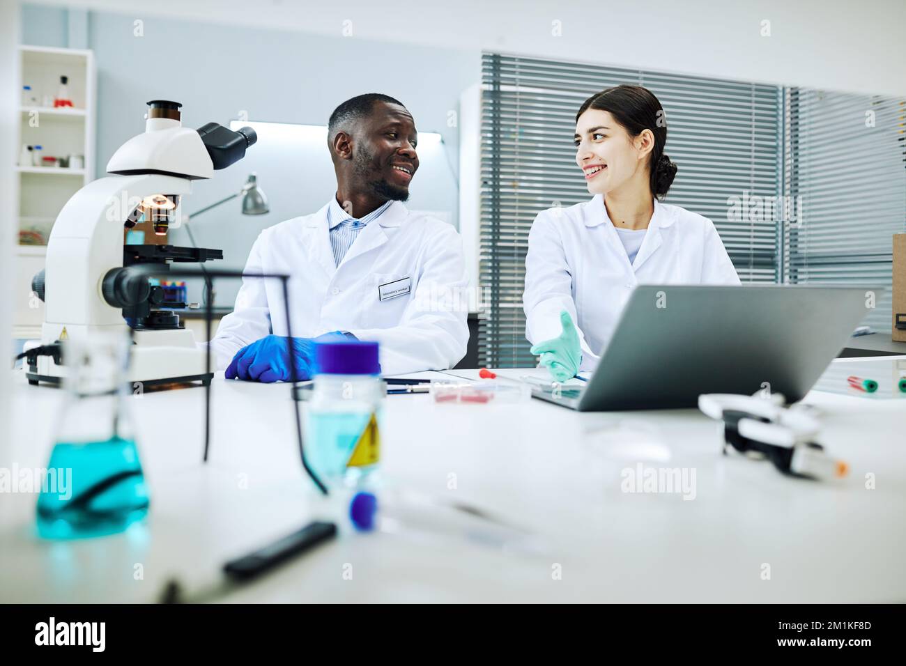 Portrait of two smiling laboratory workers looking at each other while ...