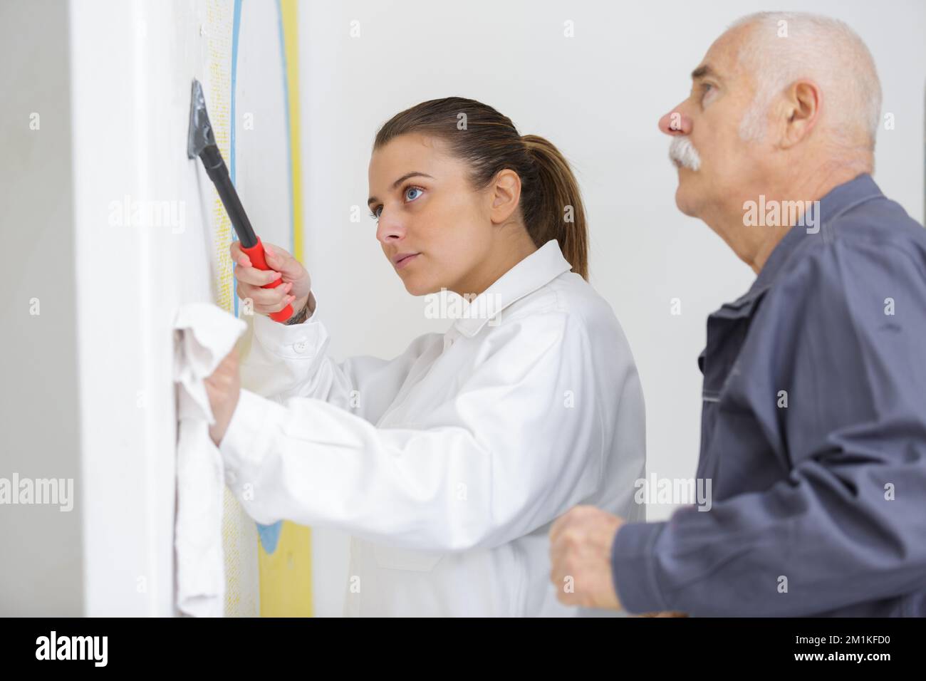 female apprentice scraping wall under supervision Stock Photo - Alamy