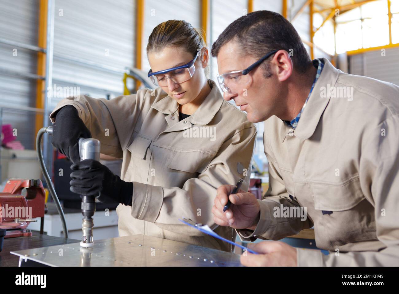 female apprentice working with a pneumatic rivet gun under supervision ...