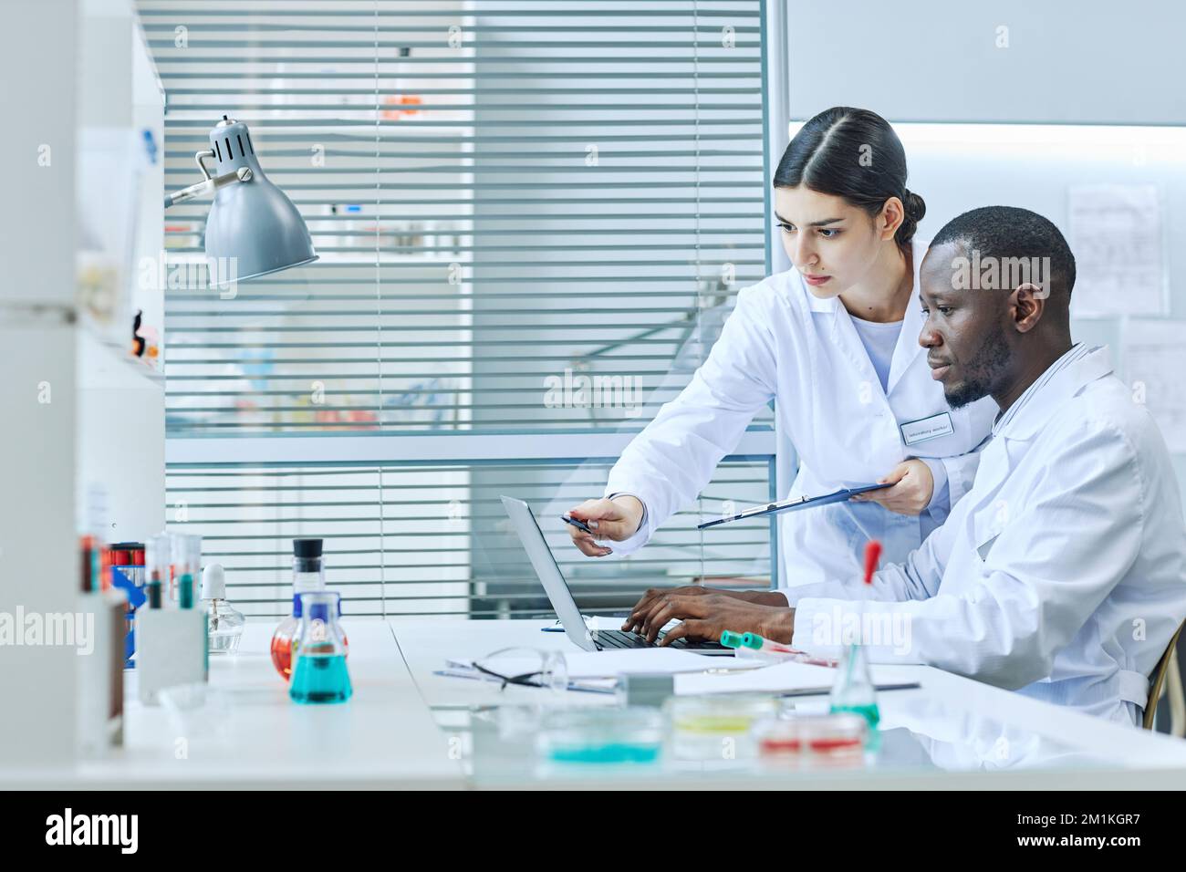 Side view portrait of two scientists using laptop in medical laboratory ...