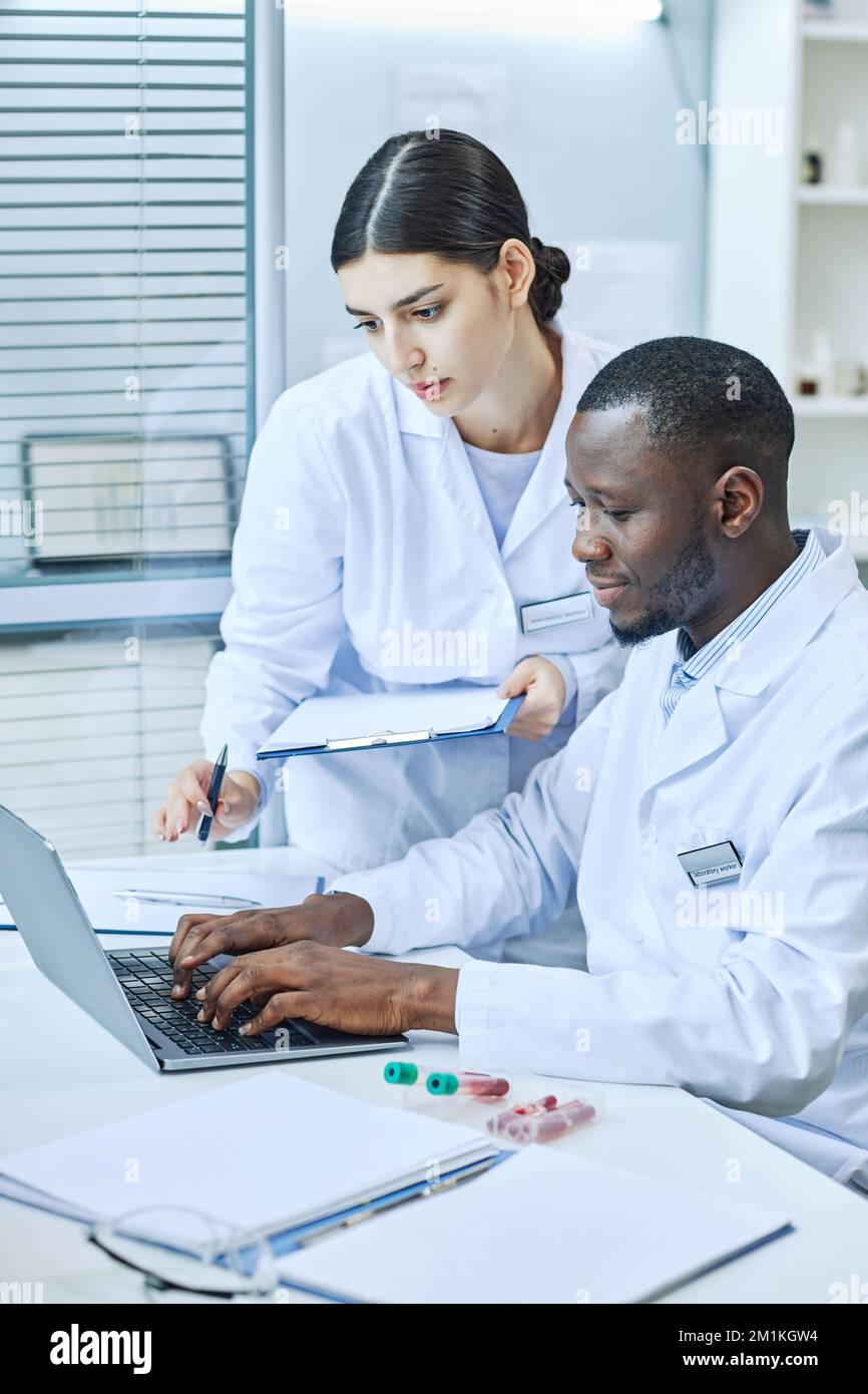 Vertical portrait of two scientists using laptop in medical laboratory ...