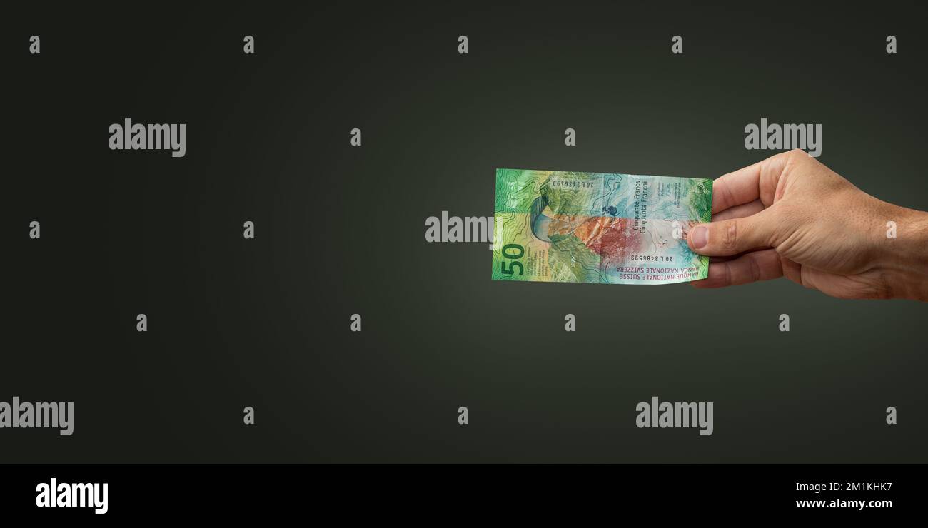 Male hand holding single bill 50 swiss franc banknote against dark ...