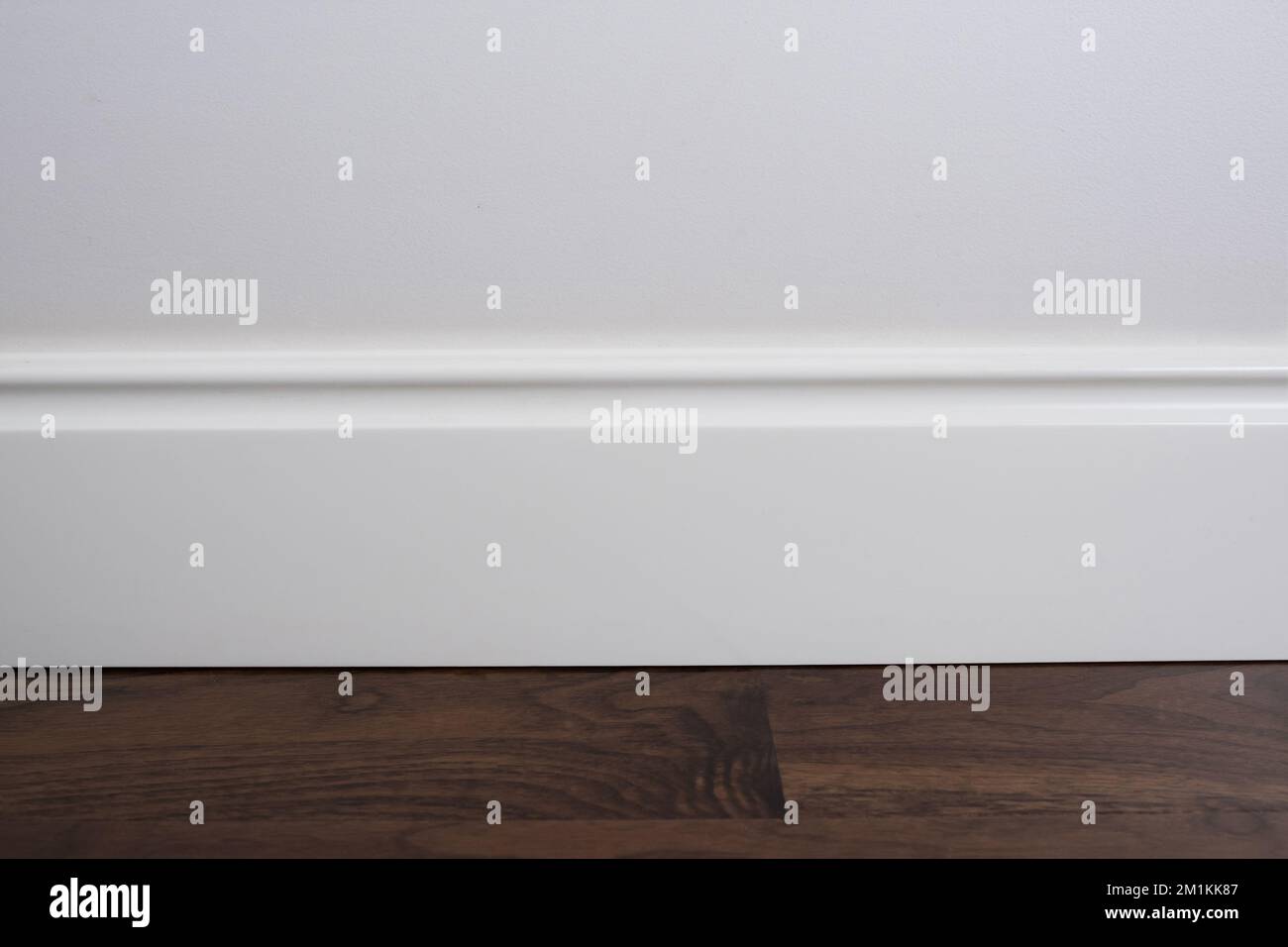 Light matte wall, white baseboard and tiles immitating hardwood ...