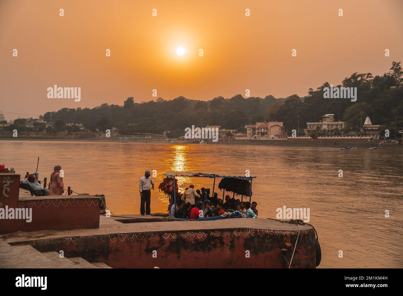 A sunset scene of a boat with people on the Ganges river in Rishikesh ...