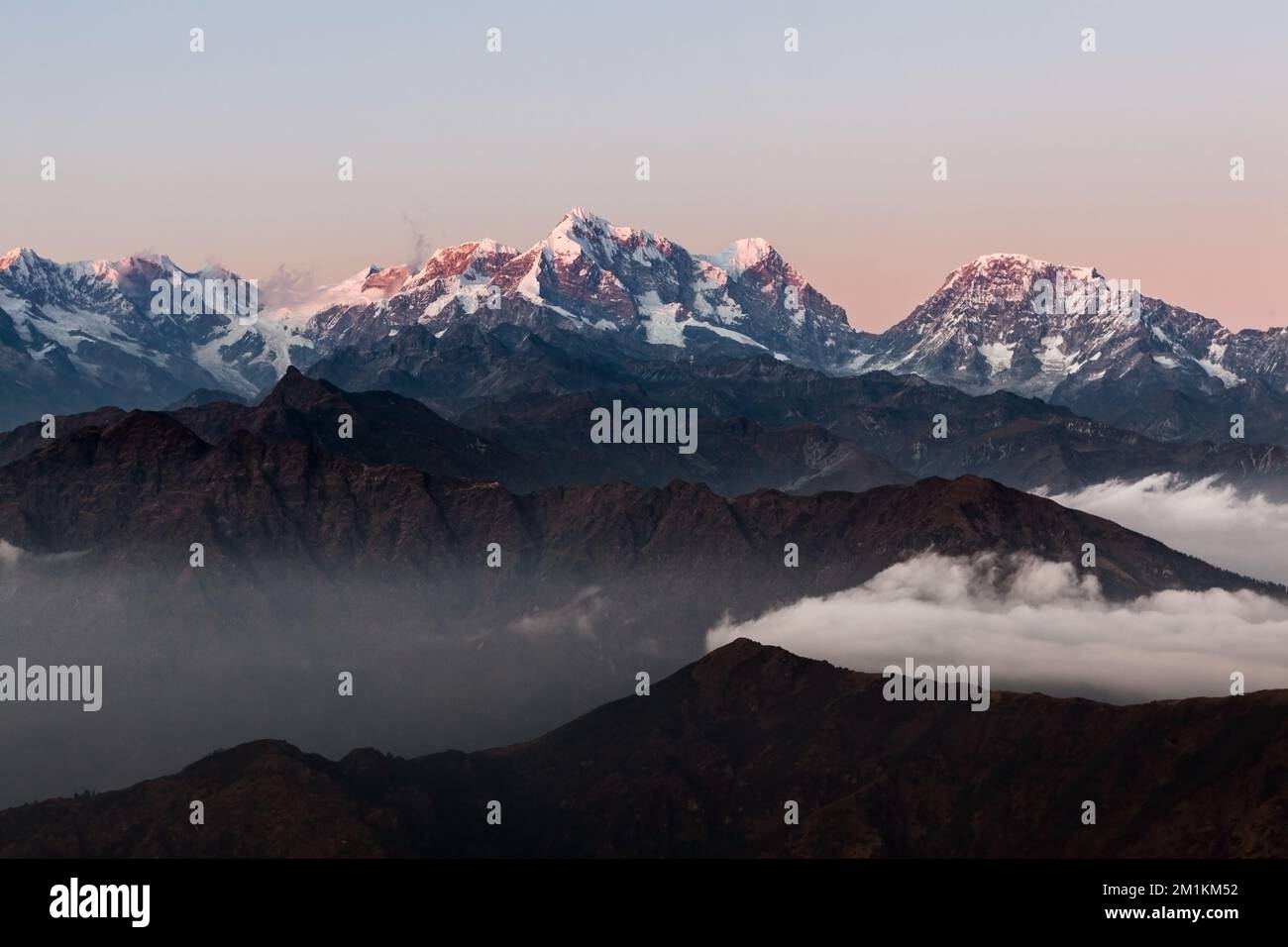 Dramatic landscape with snowy peaks rising above brown hills and morning clouds. Dramatic ...