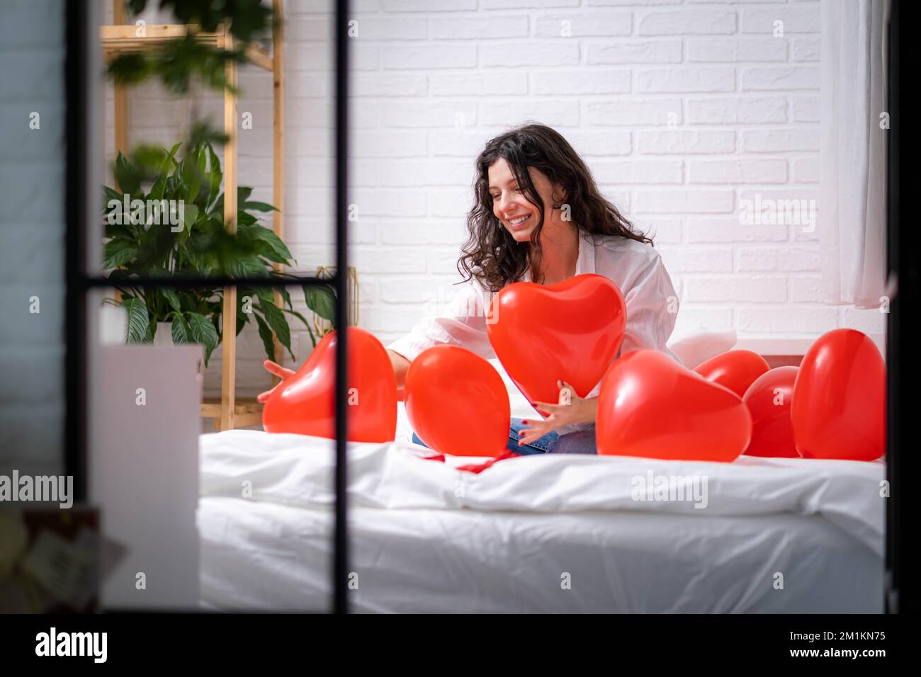 Brunette European girl rejoices playing on bed with red heart shape ...
