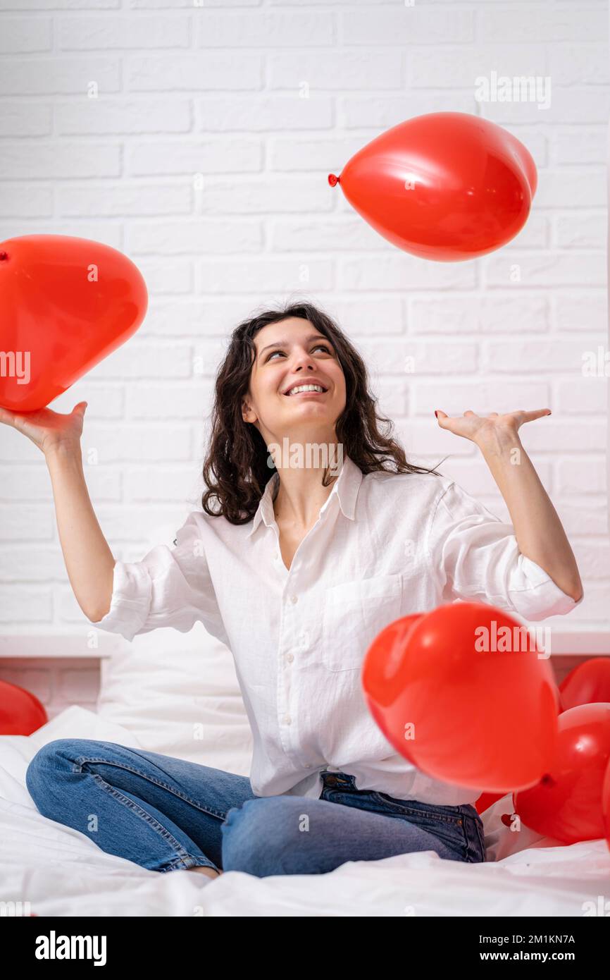 Brunette European girl rejoices playing on bed with red heart shape ...