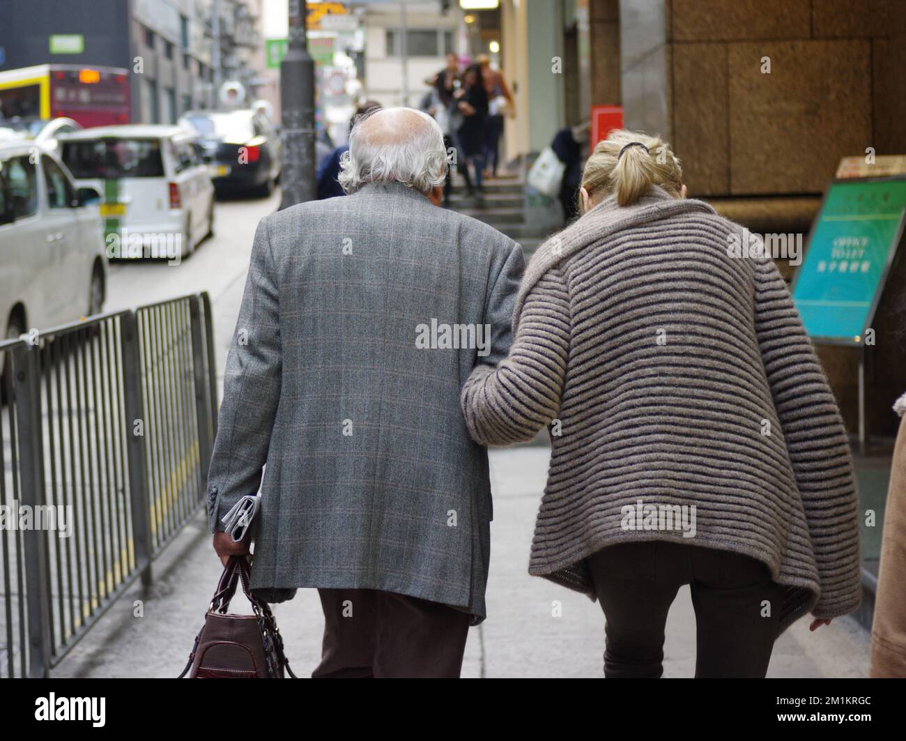 A shallow focus back view of an elderly couple walking down a sidewalk ...