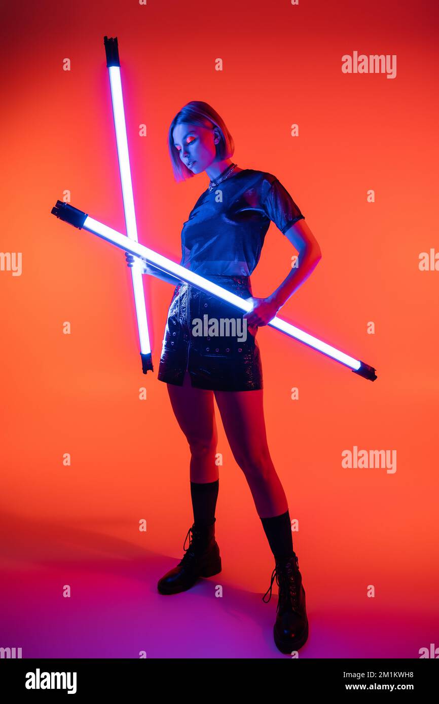full length of young woman with shining neon lamps on coral and purple ...