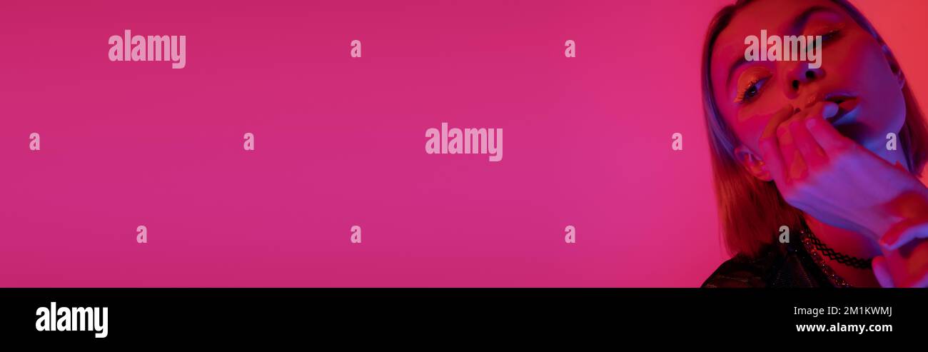 woman with neon makeup holding hand near face on deep pink background ...