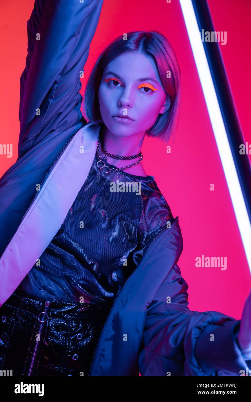 fashionable woman in neon makeup holding blue fluorescent lamp on pink ...