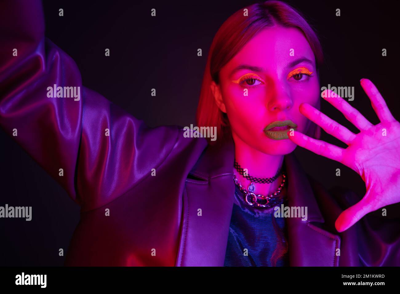 woman in leather jacket and vibrant neon makeup looking at camera on ...