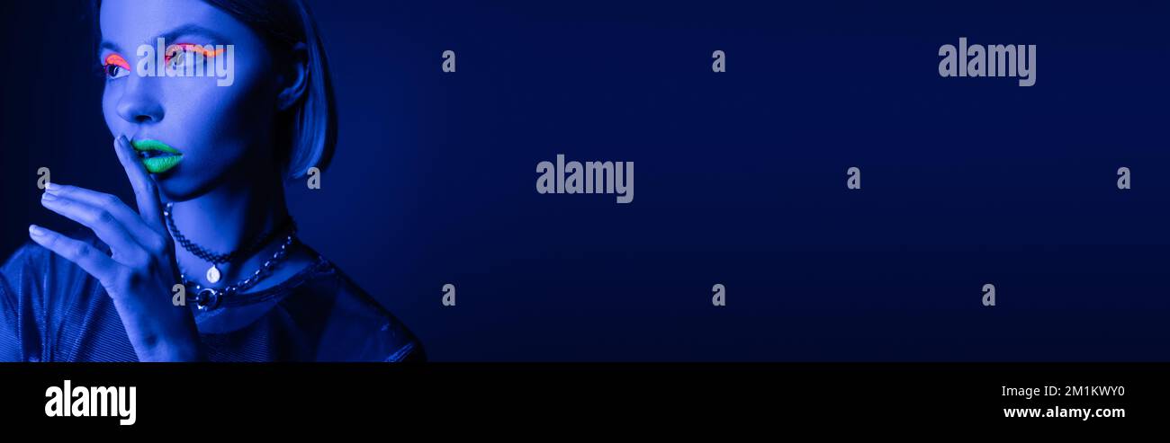 young woman with bright neon visage touching green lips and showing ...