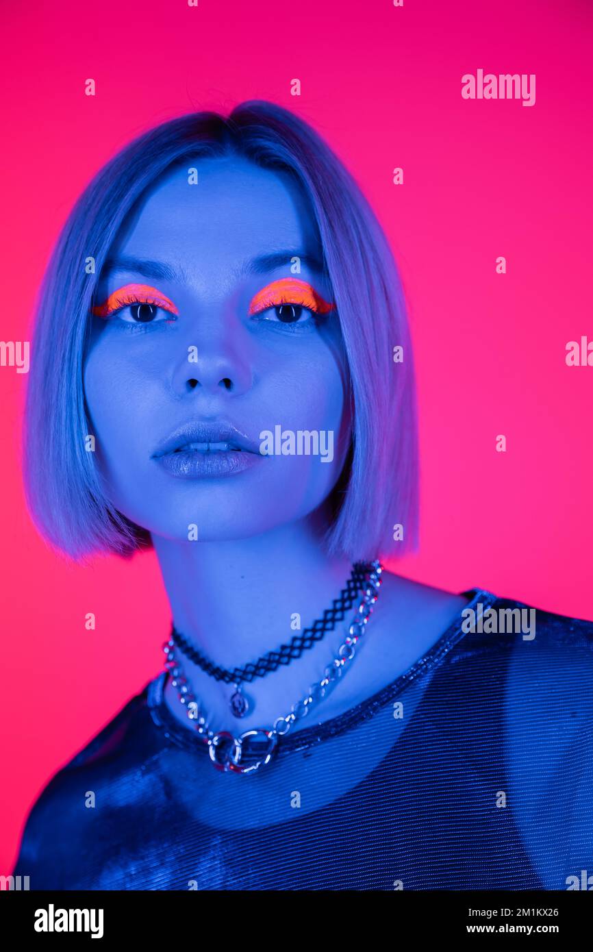 portrait of young woman with neon makeup looking at camera in blue ...