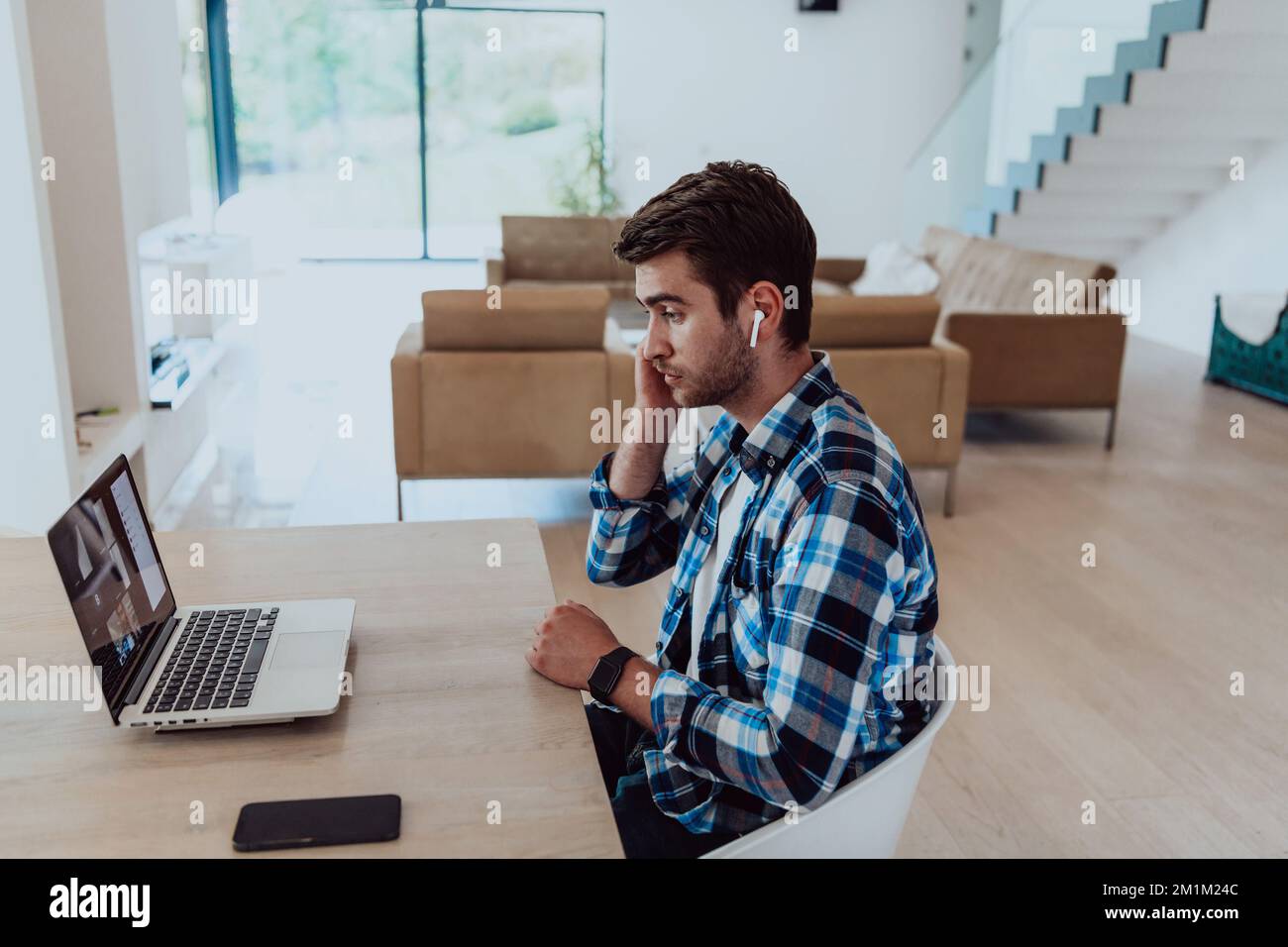 The man sitting at a table in a modern living room, with headphones ...