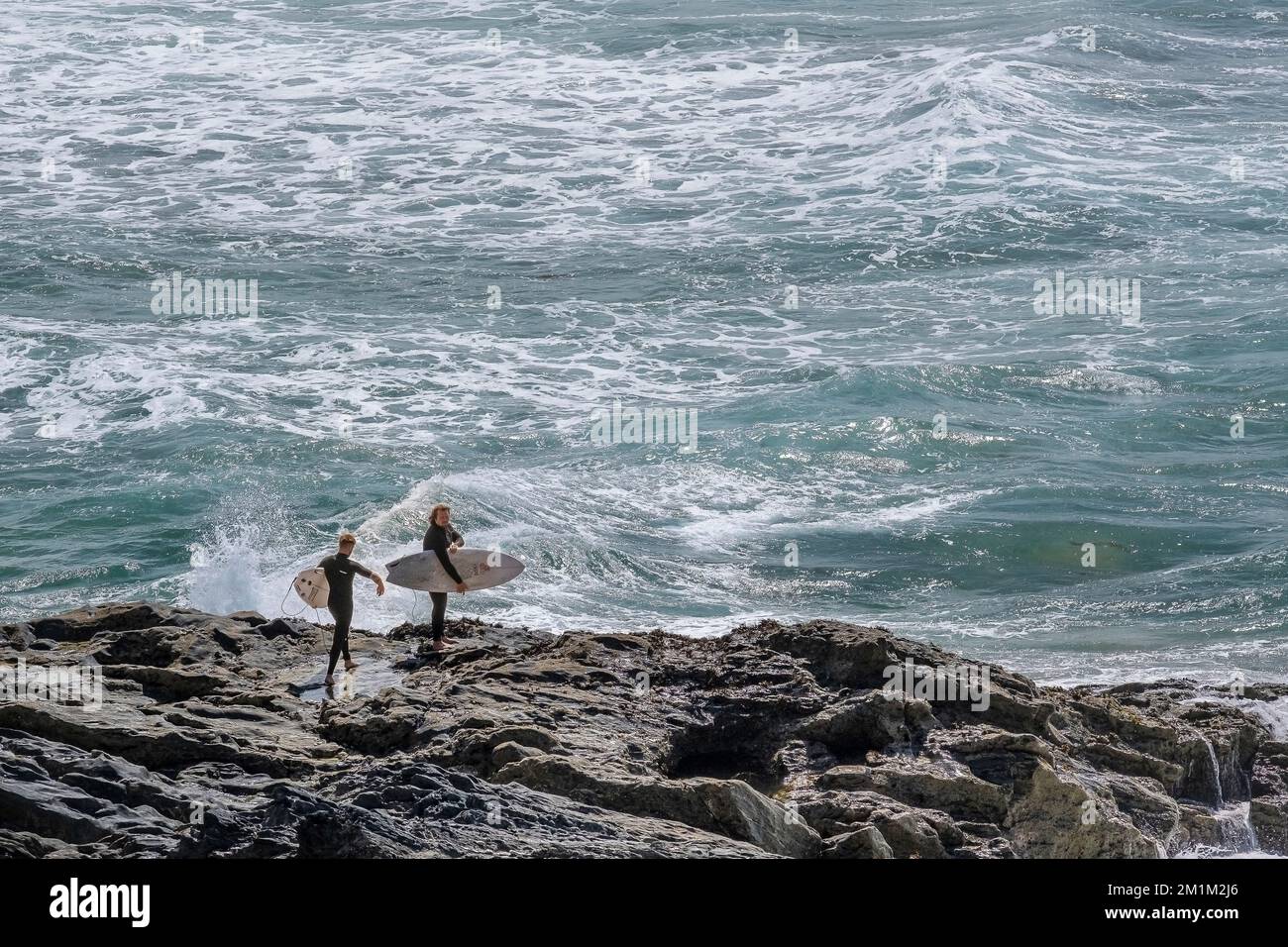 Surfers carrying their surfboards walking along rocks at Pentire Point ...