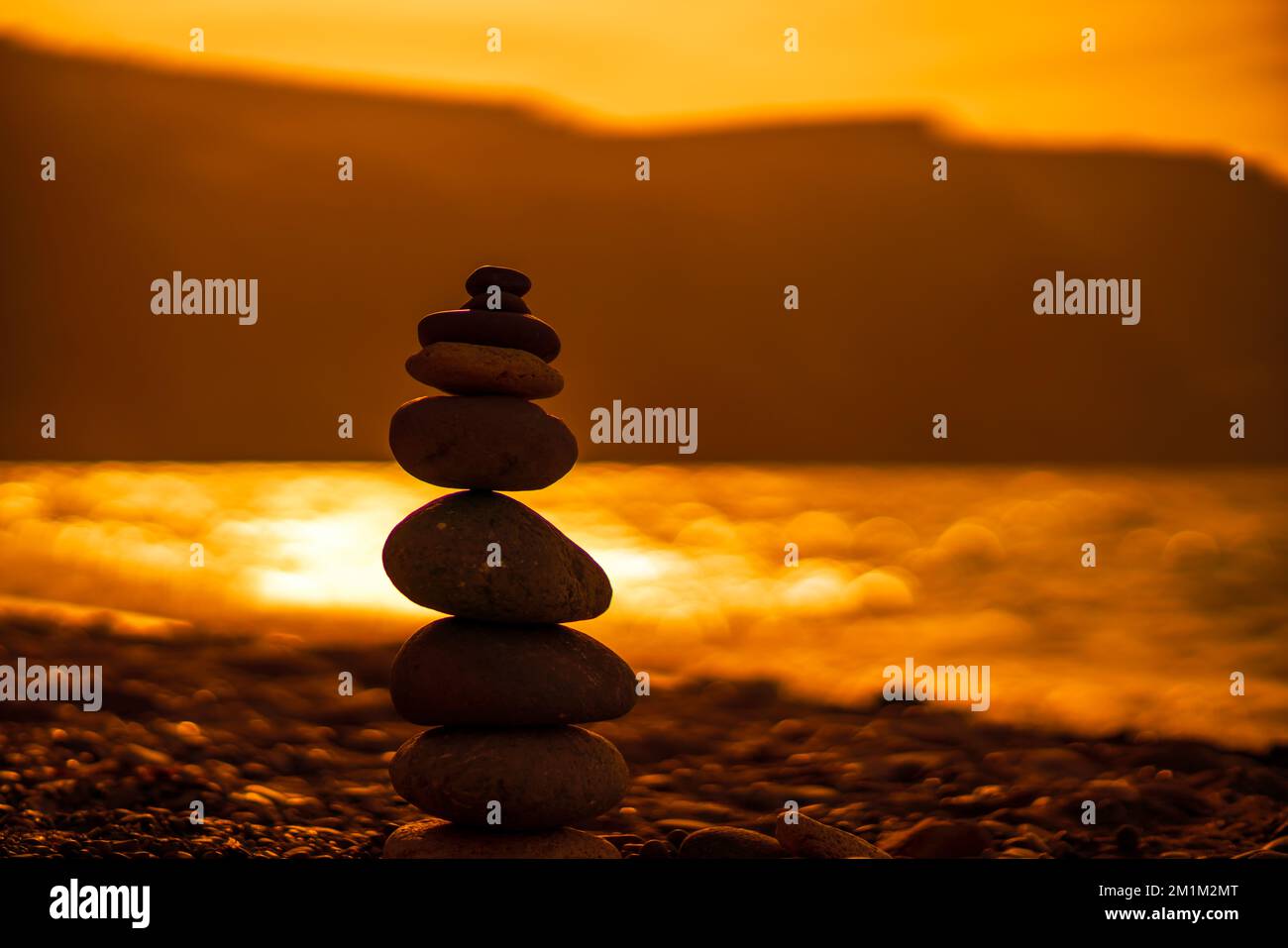 Pebble pyramid silhouette on the beach. Sunset with sea in the ...