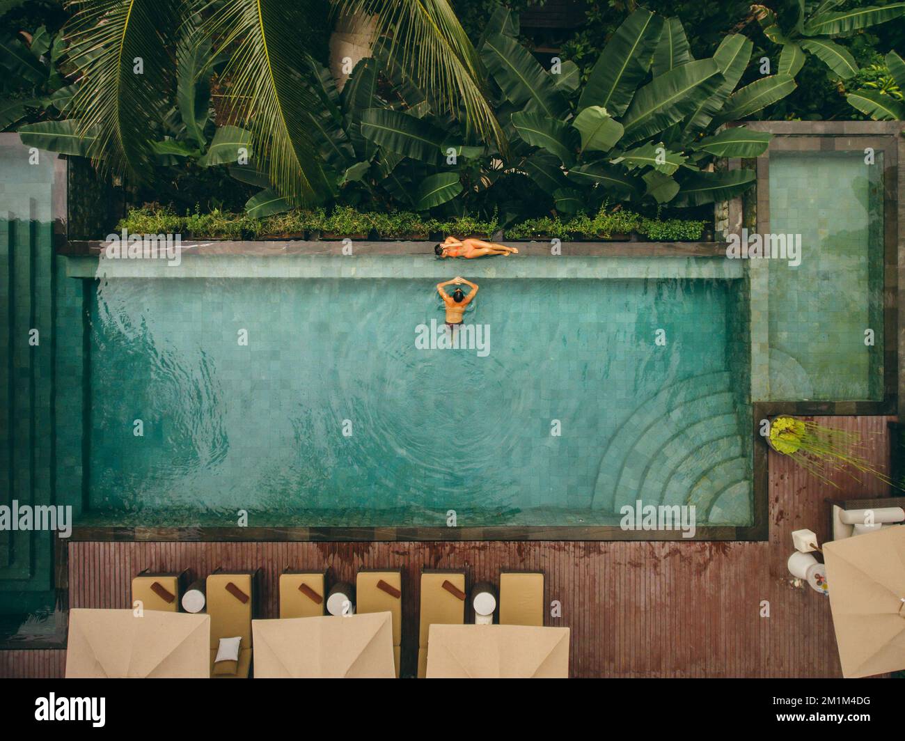 Aerial shot of woman relaxing at the poolside with man in swimming pool ...