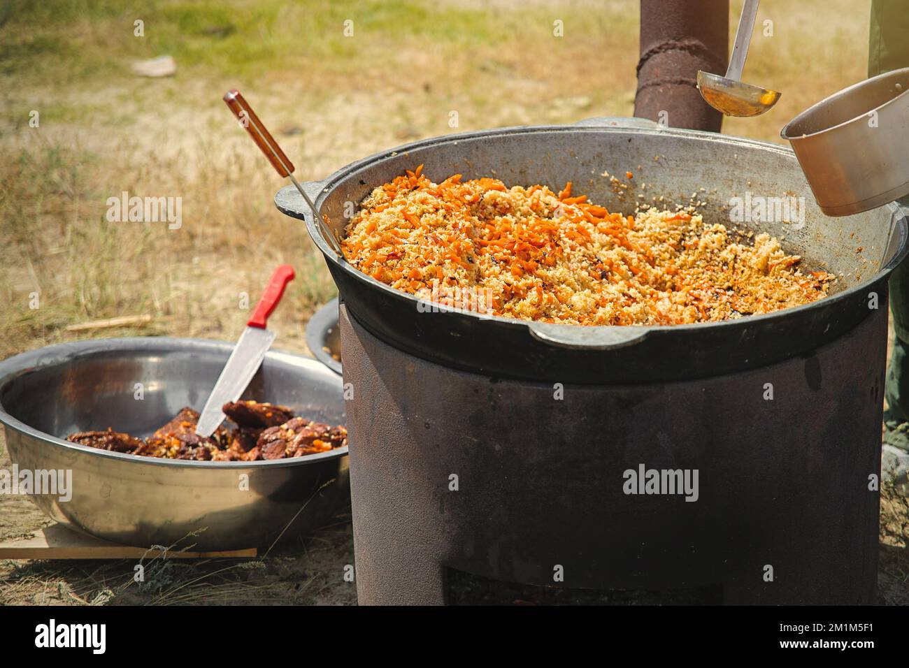 Cooking traditional oriental pilaf in big cauldron on a sunny day ...